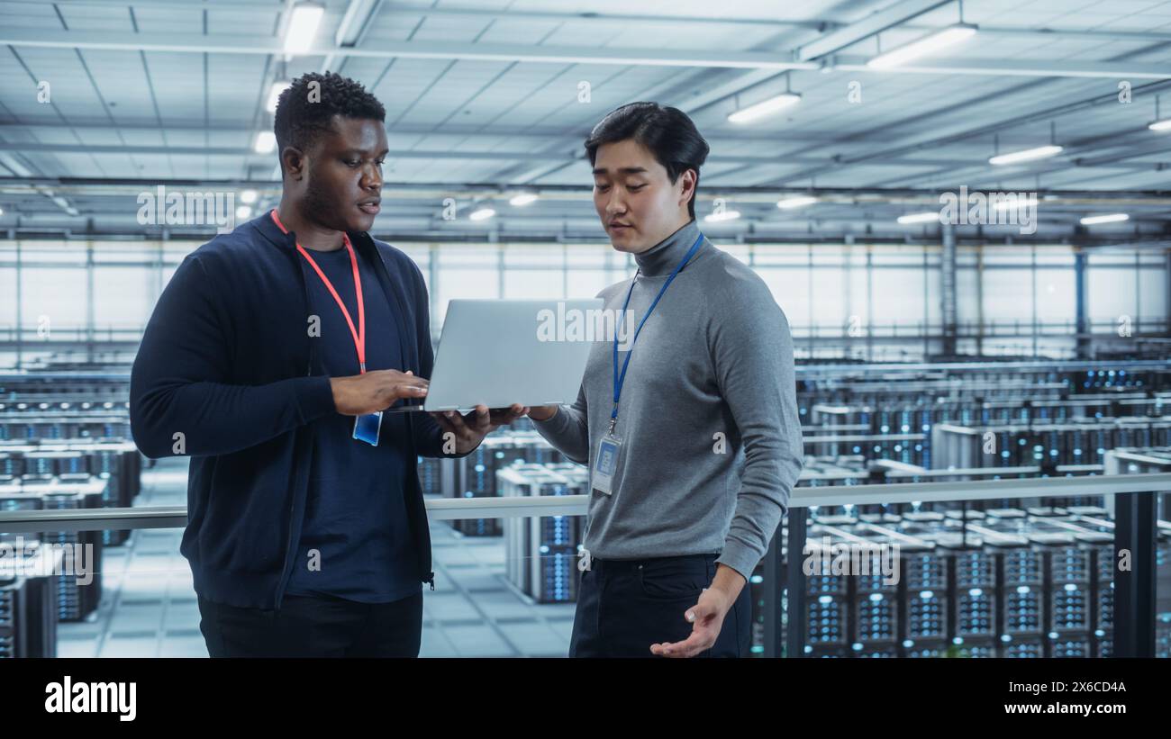 Two Multiethnic Male Data Center System Administrators and IT Specialists Talk, Use Laptop ...