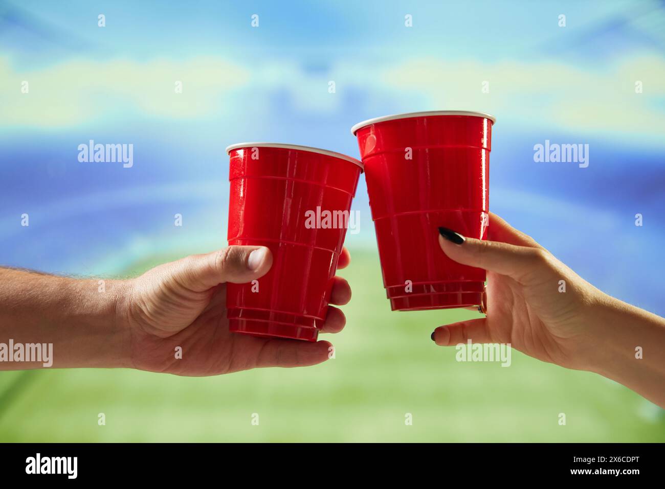 Hands holding red mugs with beer and clicking with blurred sport open ...