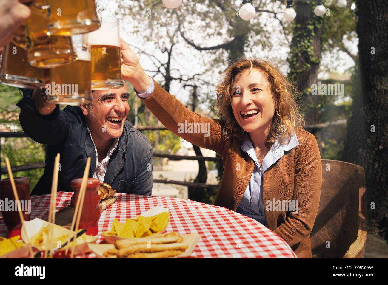 Group of friends toasting with beer in an outdoor setting, smiling and ...