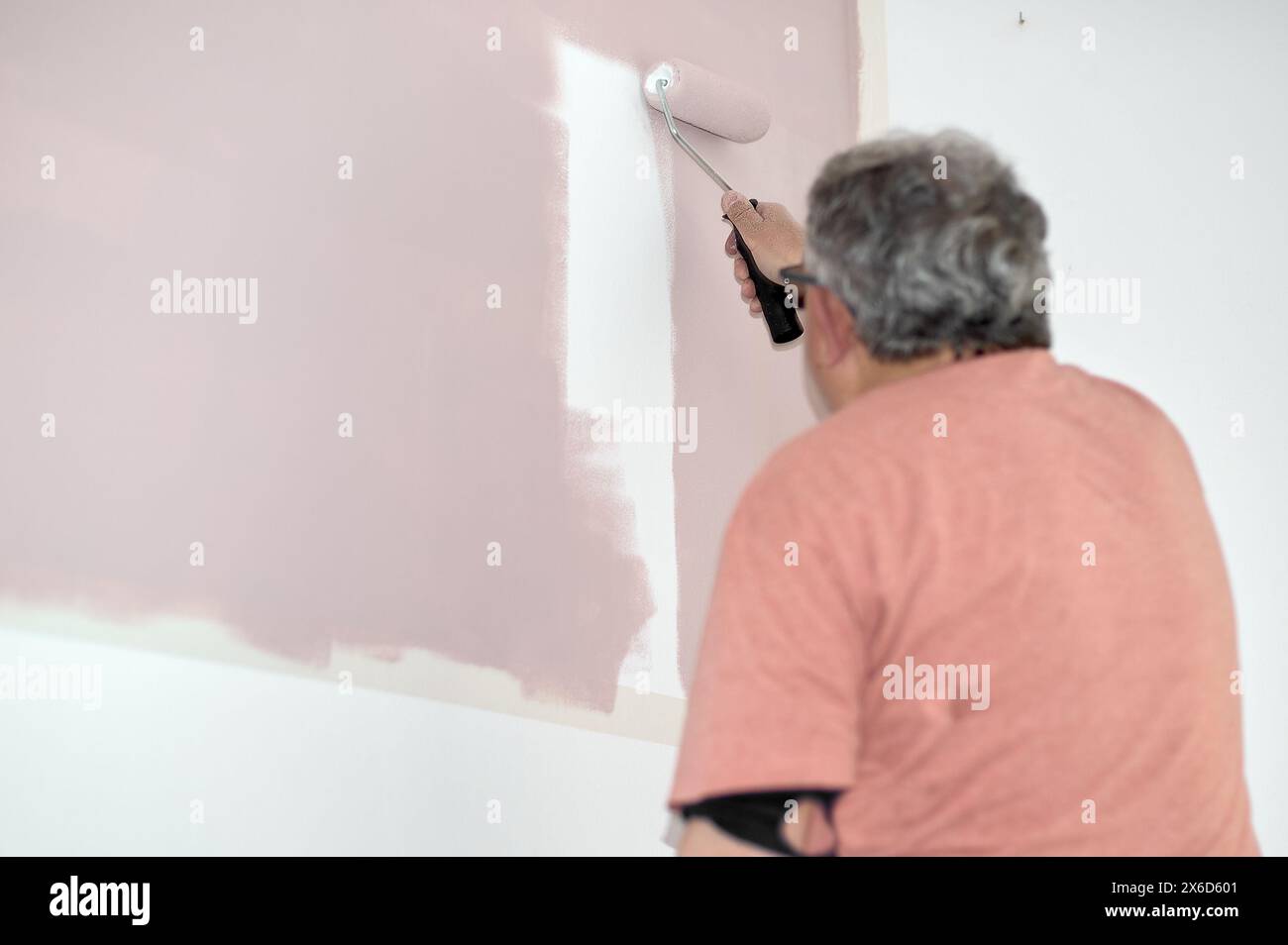 An older man is painting a wall in his home with a roller. The fresh ...