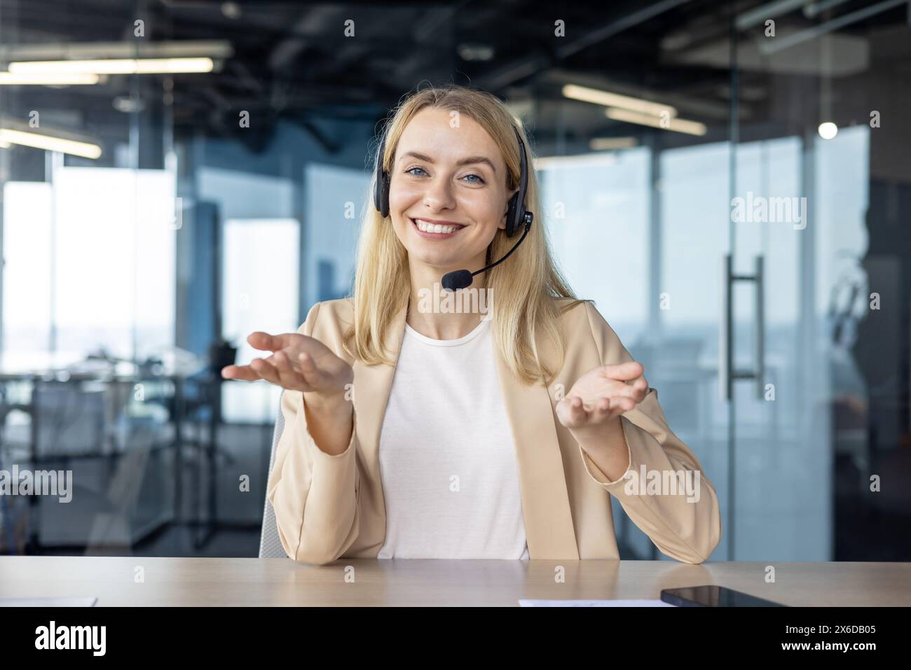Smiling customer service representative wearing a headset while sitting at a desk in a modern ...
