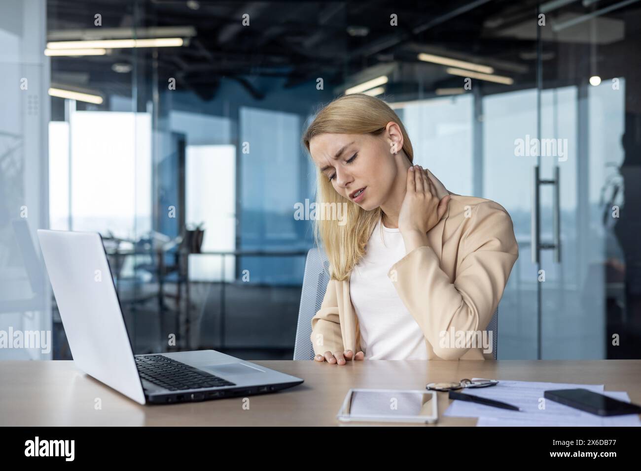 Young businesswoman feeling neck pain while working on laptop at office ...