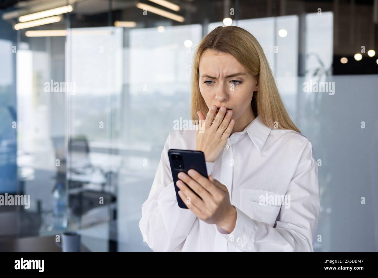 A young businesswoman stands in a modern office, shocked and concerned ...