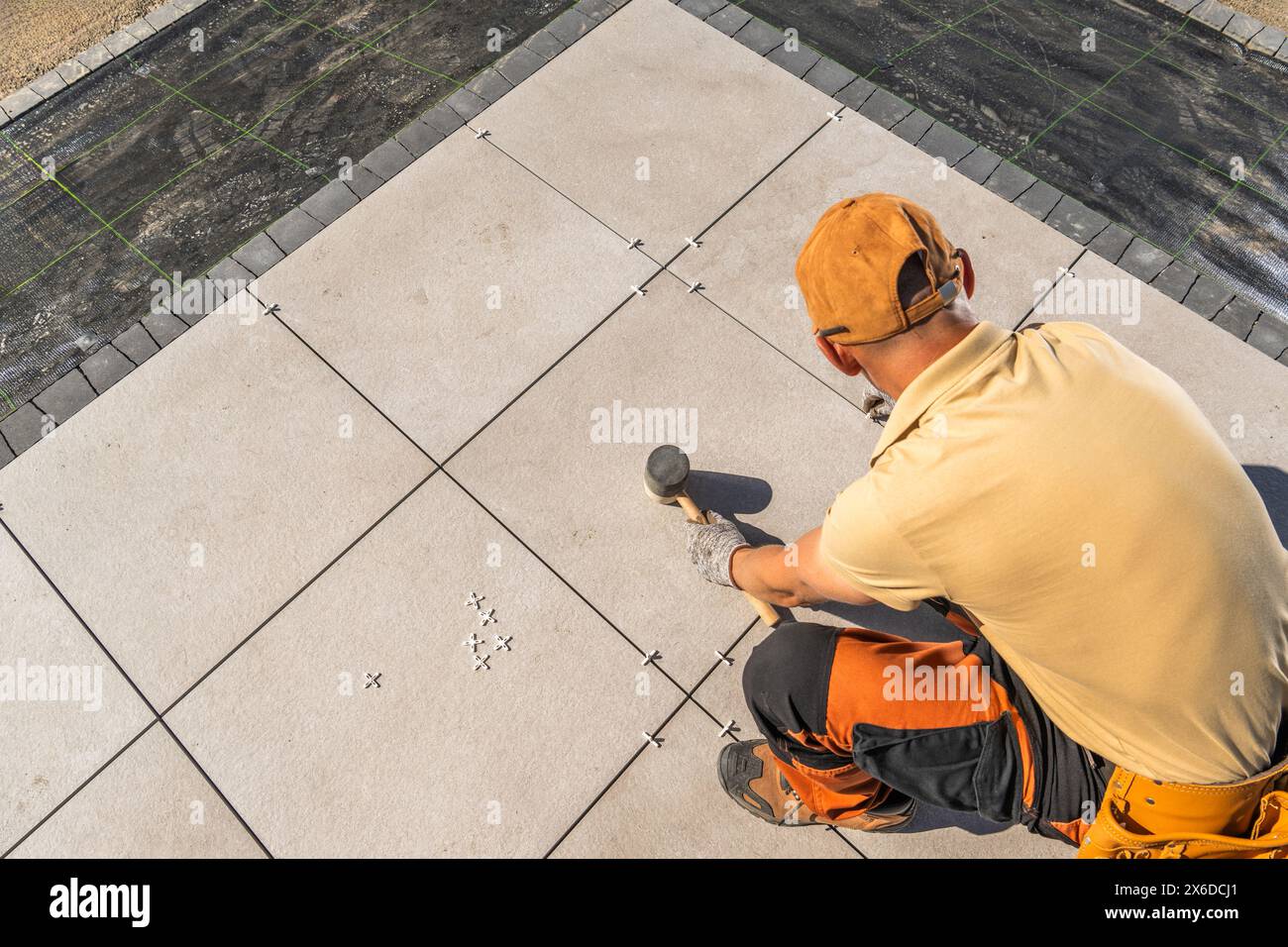 Caucasian worker is installing tiles on a concrete garden patio floor ...
