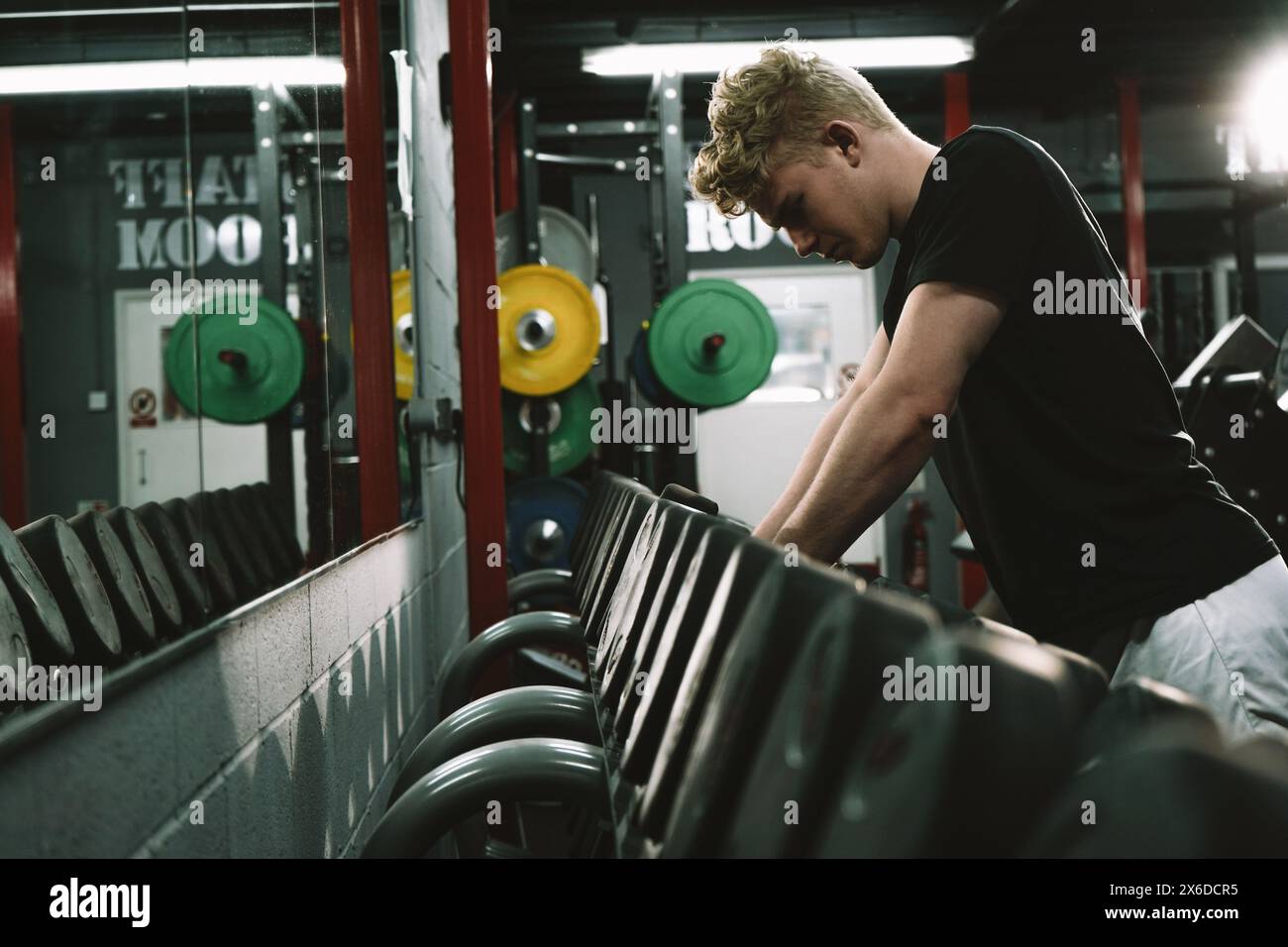 Athletic man resting between dumbbell workout sets at the gym, leaning ...
