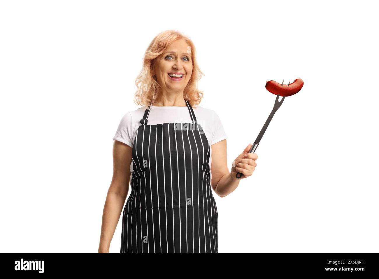 Middle aged woman wearing an apron and holding a sausage on a fork ...