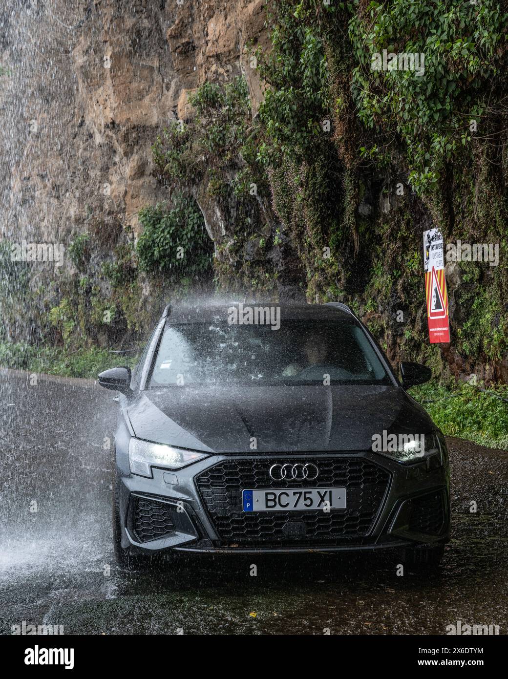 Car on a mountainside road driving under the extreme natural waterfall ...