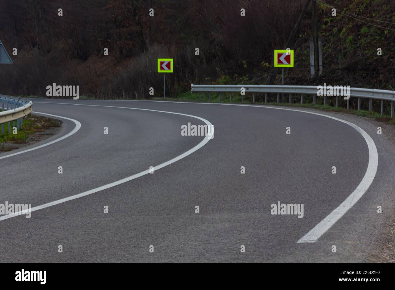 Asphalt road with bright traffic signs in situ of the sharp left turn ...