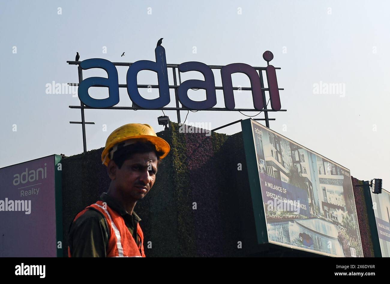 A construction worker walks below the Adani logo near a building ...