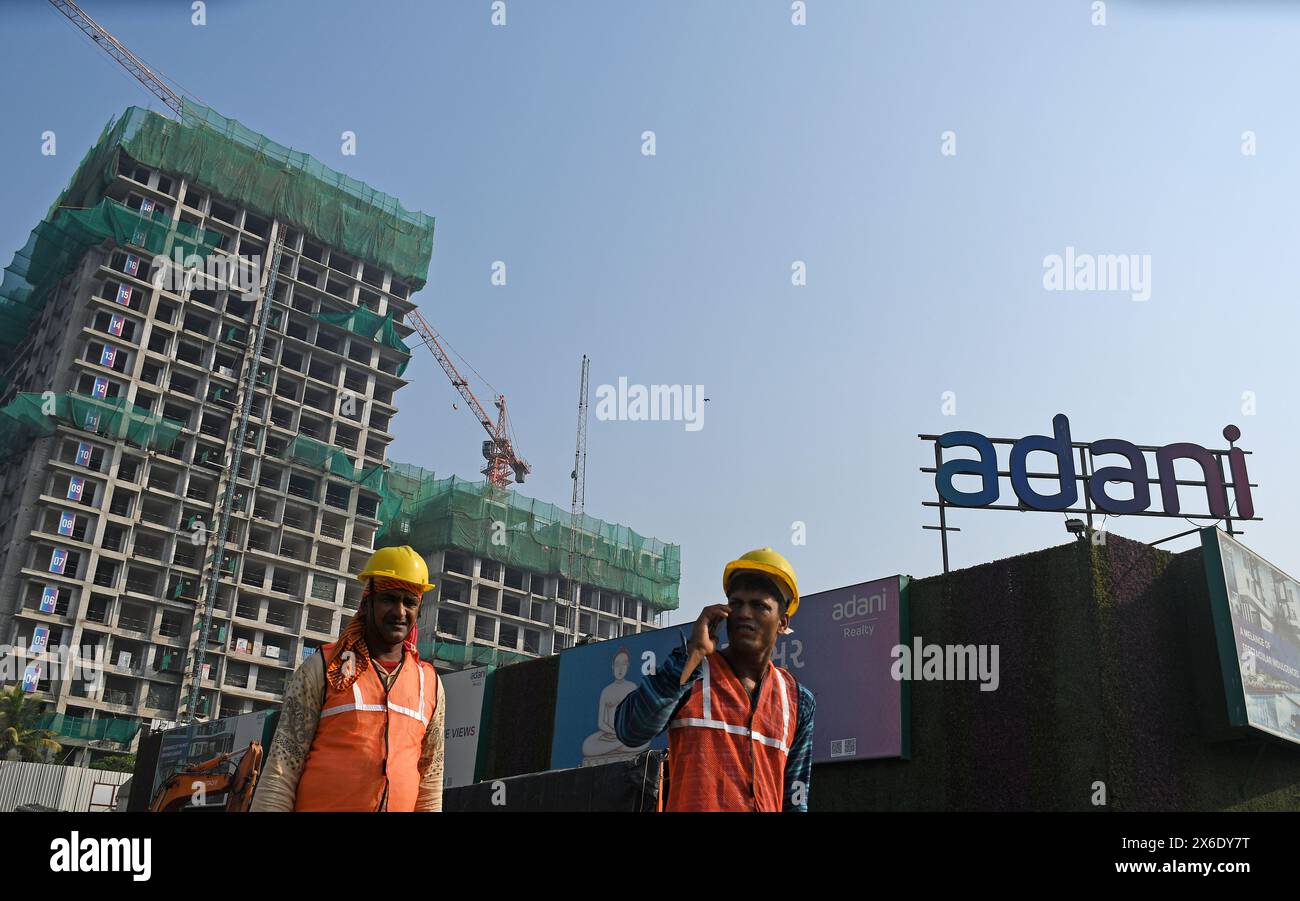 Construction workers walk below the Adani logo near a building ...