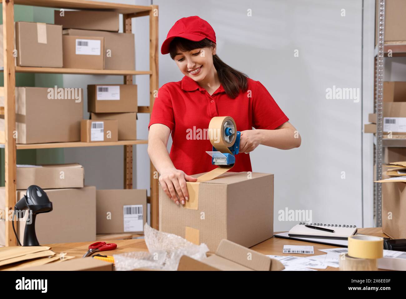 Parcel packing. Post office worker taping box at wooden table indoors ...