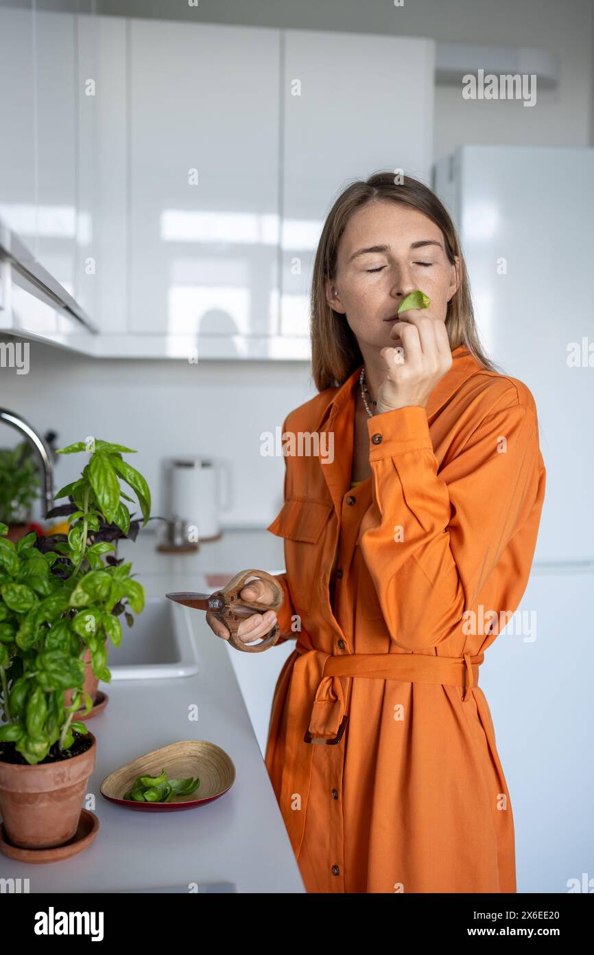 Woman sniffs home-grown basil leaf. Female gardener enjoying smell of ...