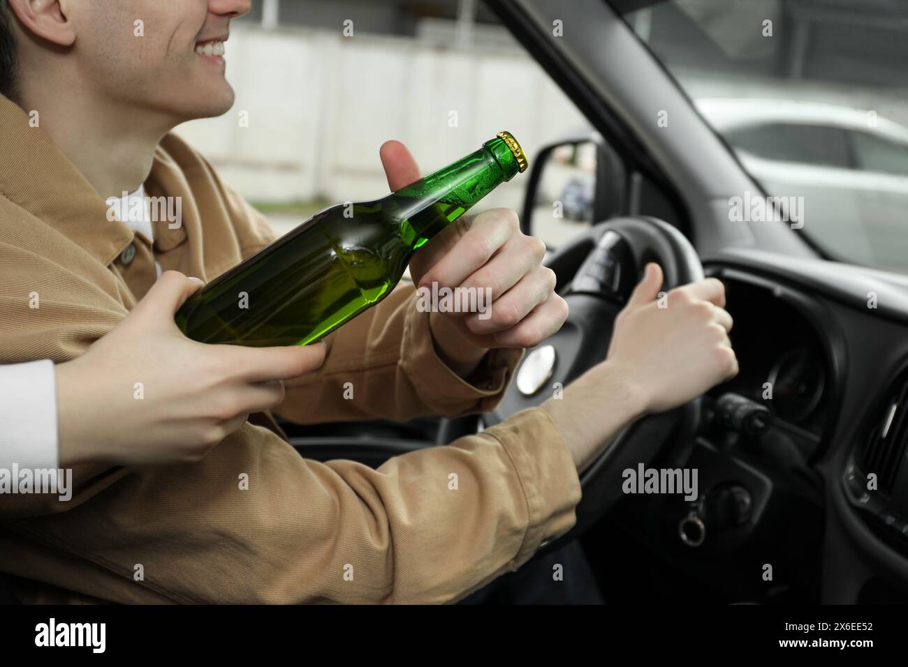 Smiling man taking bottle of beer while driving car, closeup. Don't ...