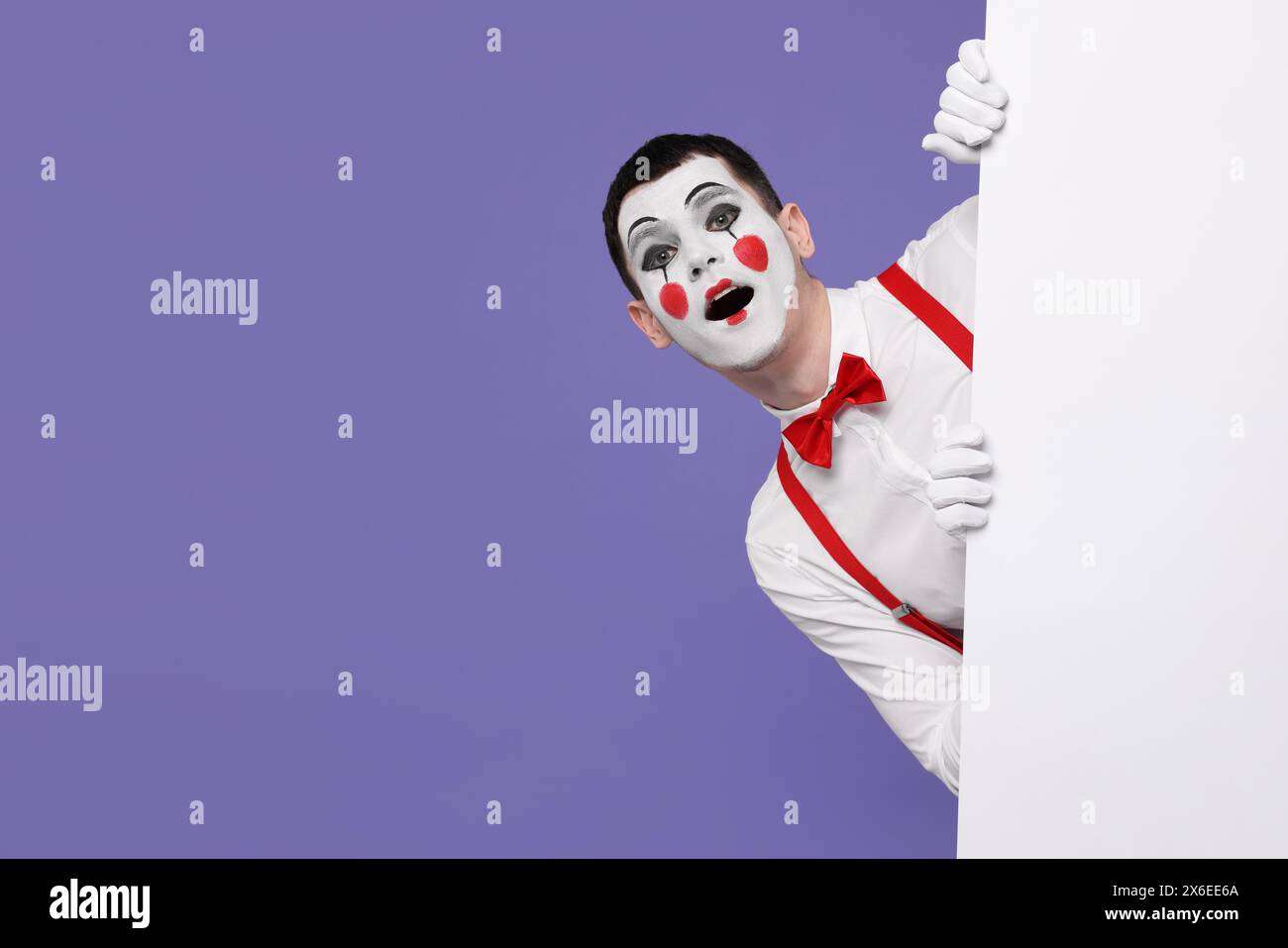 Funny mime artist peeking out of blank poster on purple background ...