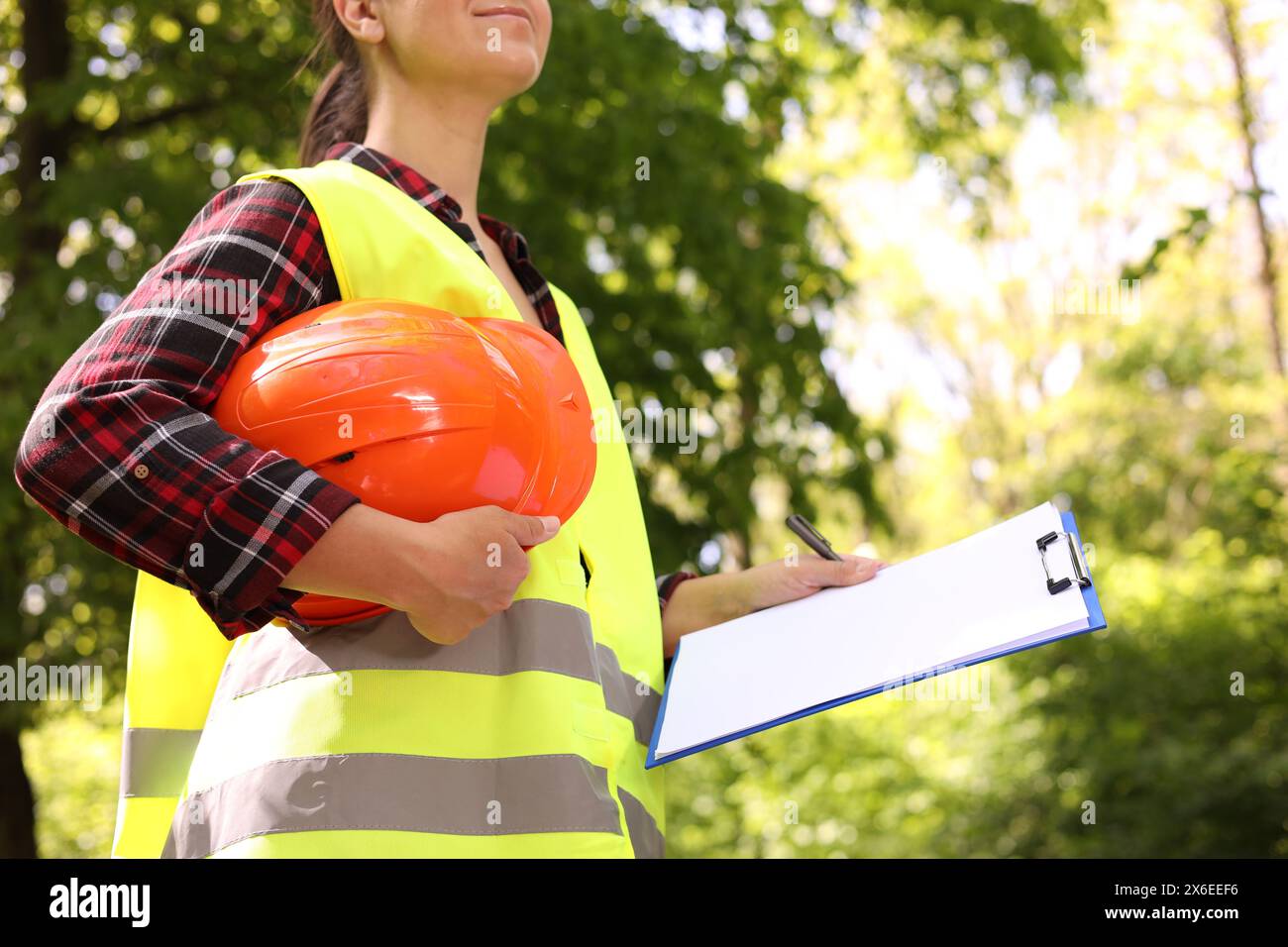 Forester with hard hat and clipboard examining plants in forest ...
