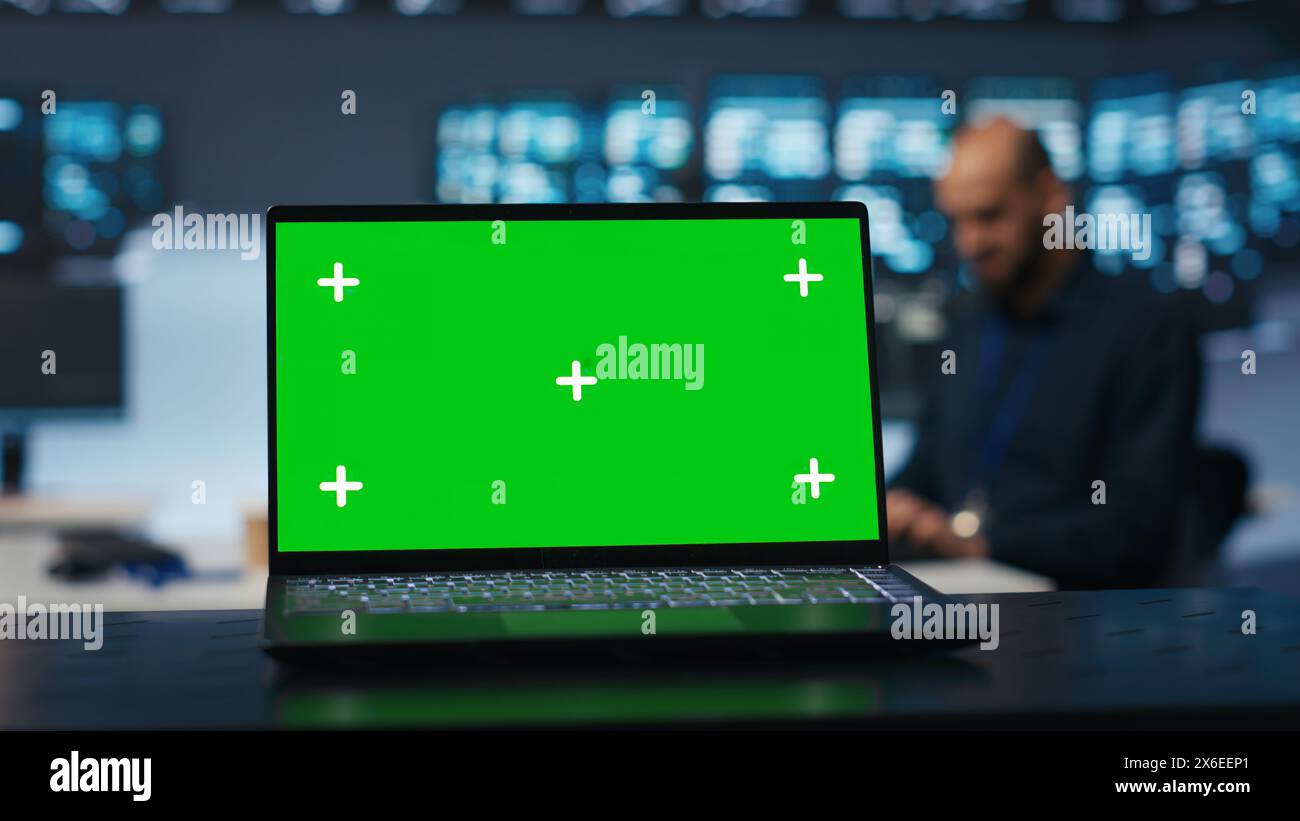 Focus on green screen laptop in server room used by man in blurry ...