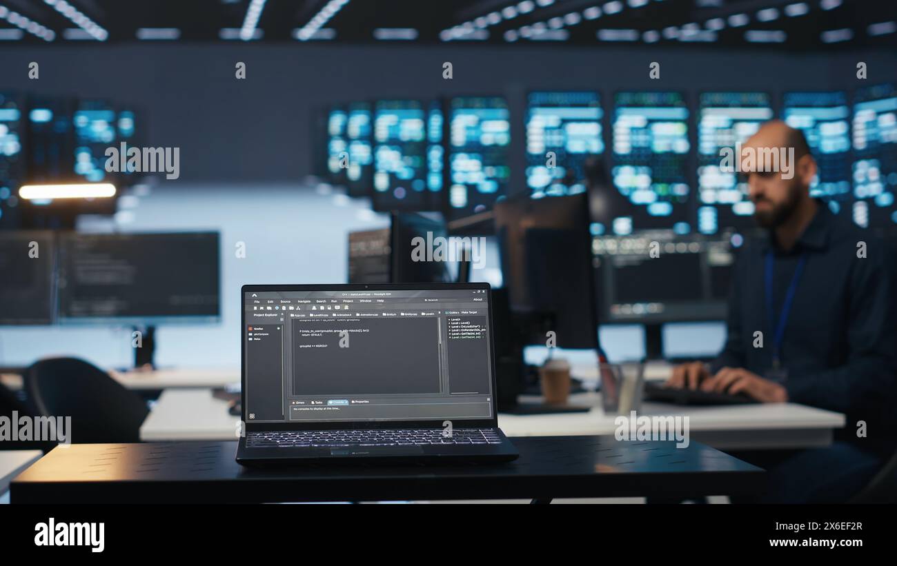 Focus on laptop used by programmer running code in blurry background for data center servers ...
