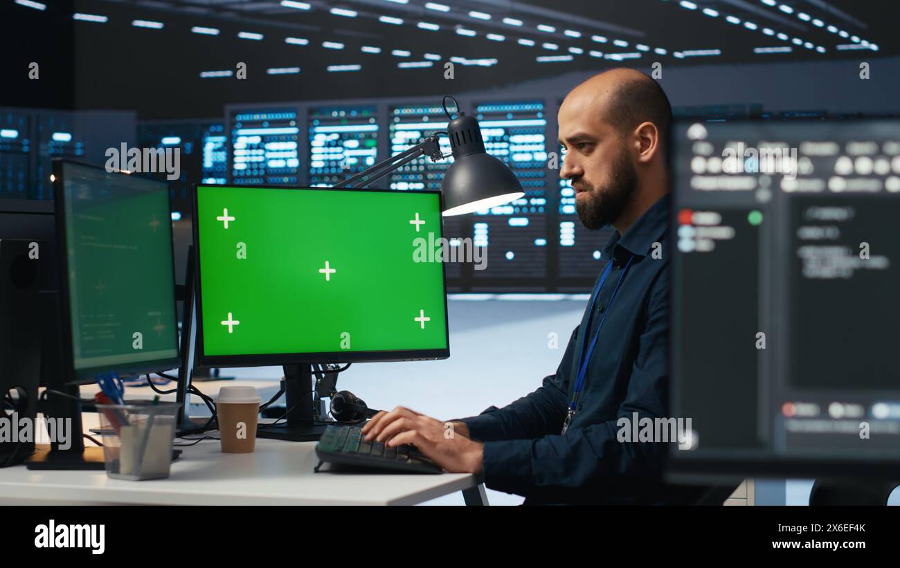 Technician overseeing server room, running code on green screen computer, troubleshooting ...