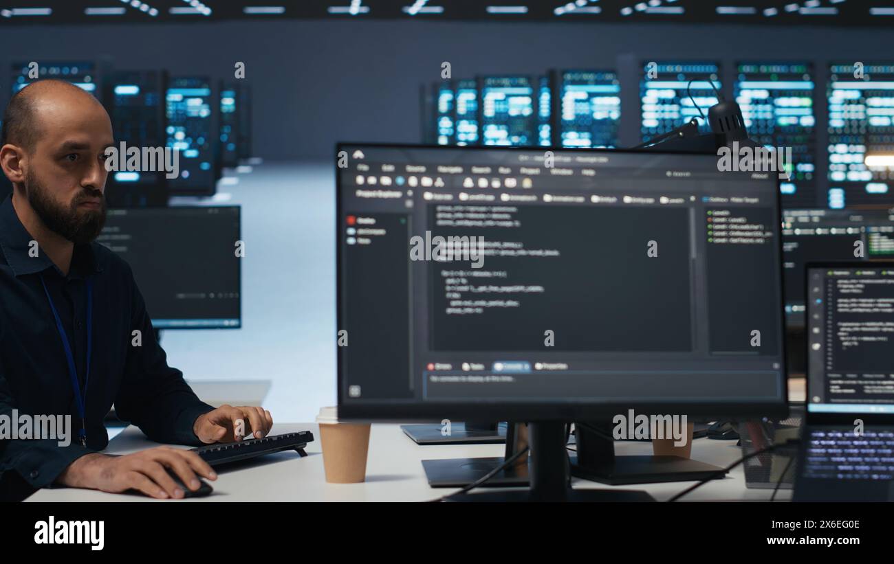 Engineer writing code in high tech facility with server rows providing computing resources for ...