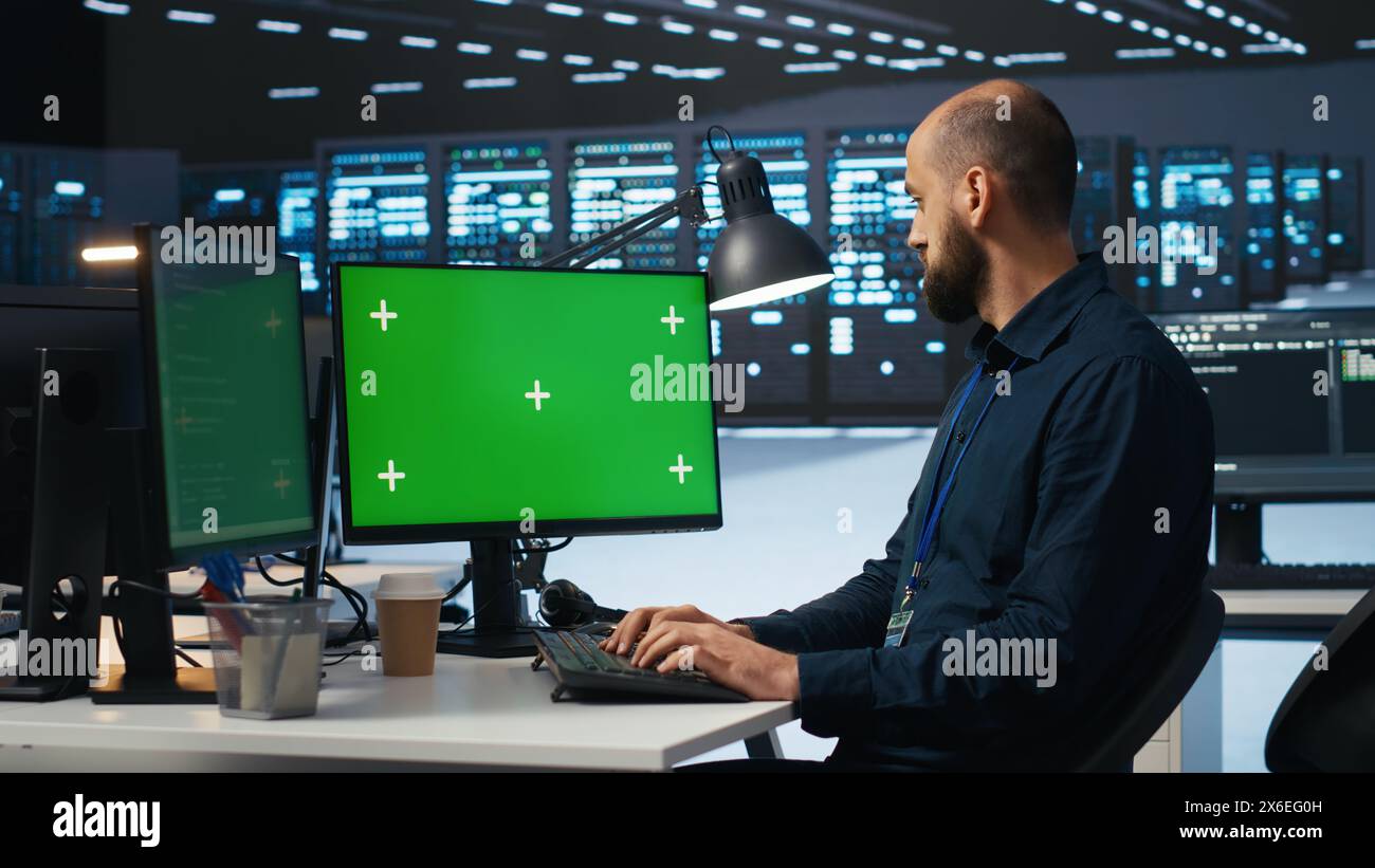 Man typing code on green screen computer in high tech data center with server rows providing ...