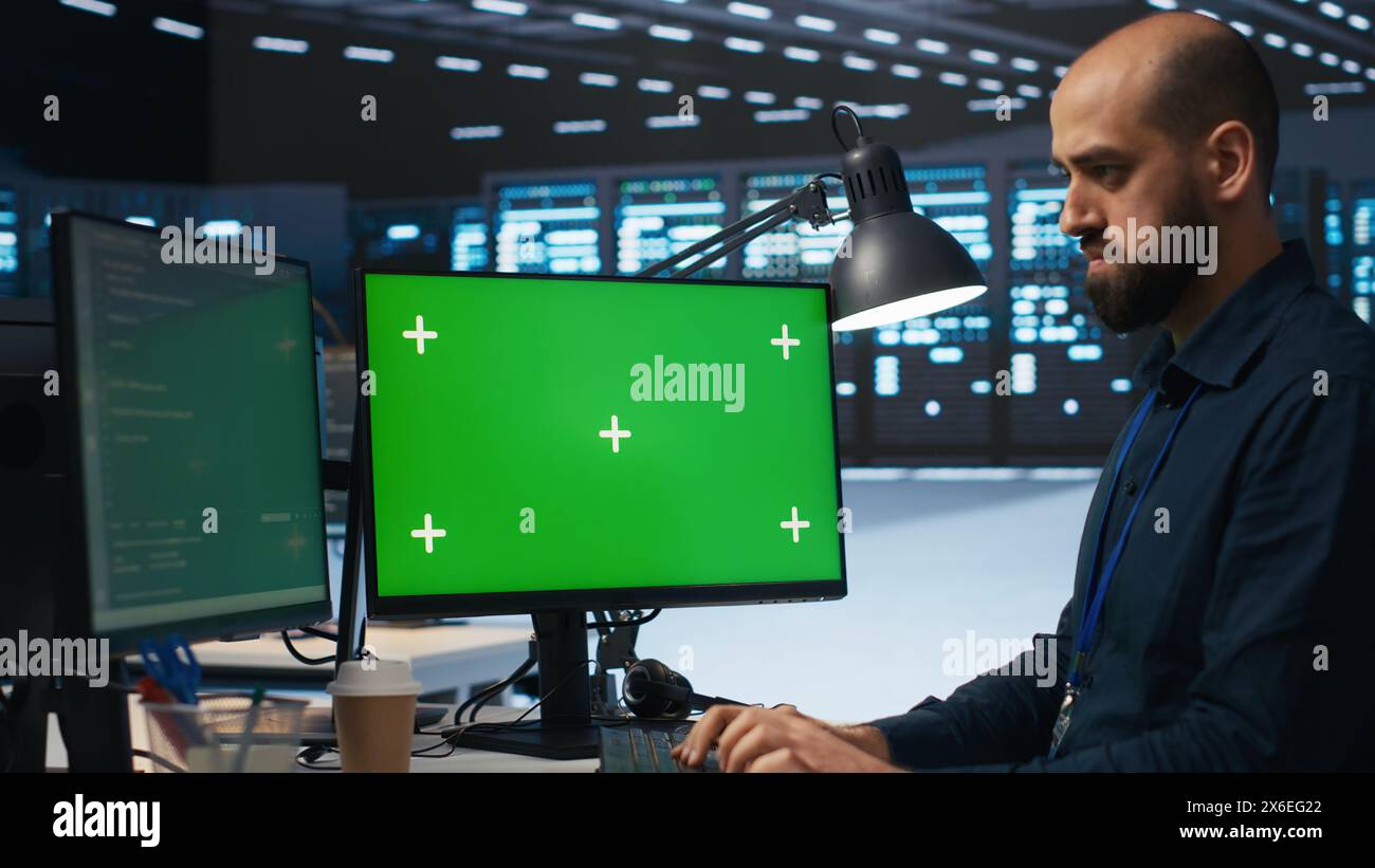 System administrator working on green screen computers in data center, ensuring optimal ...