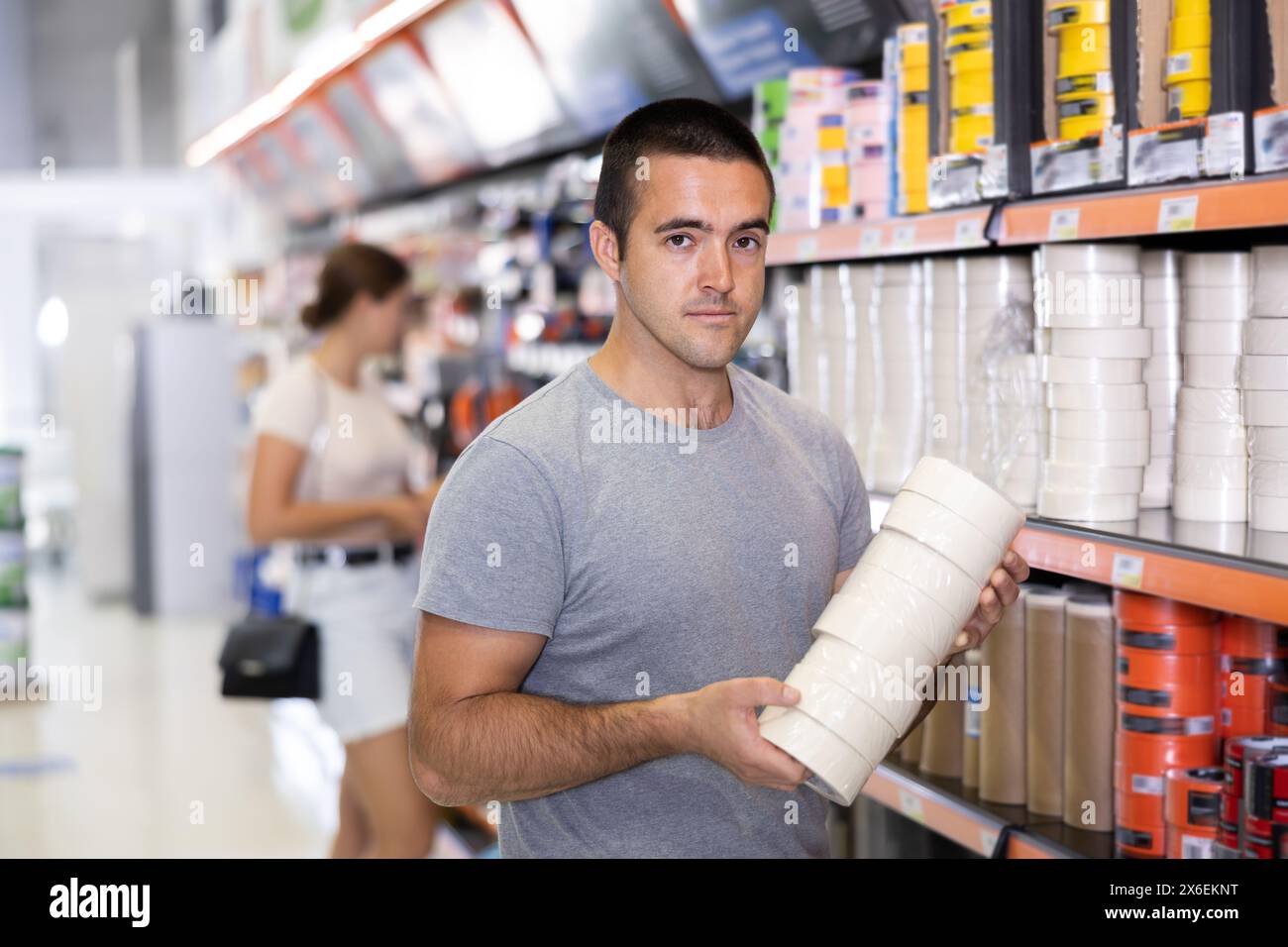 Skilled young handyman choosing painter tape in hardware store Stock ...