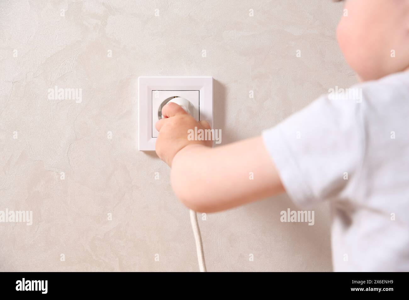 Little child playing with electrical socket and plug indoors, closeup ...