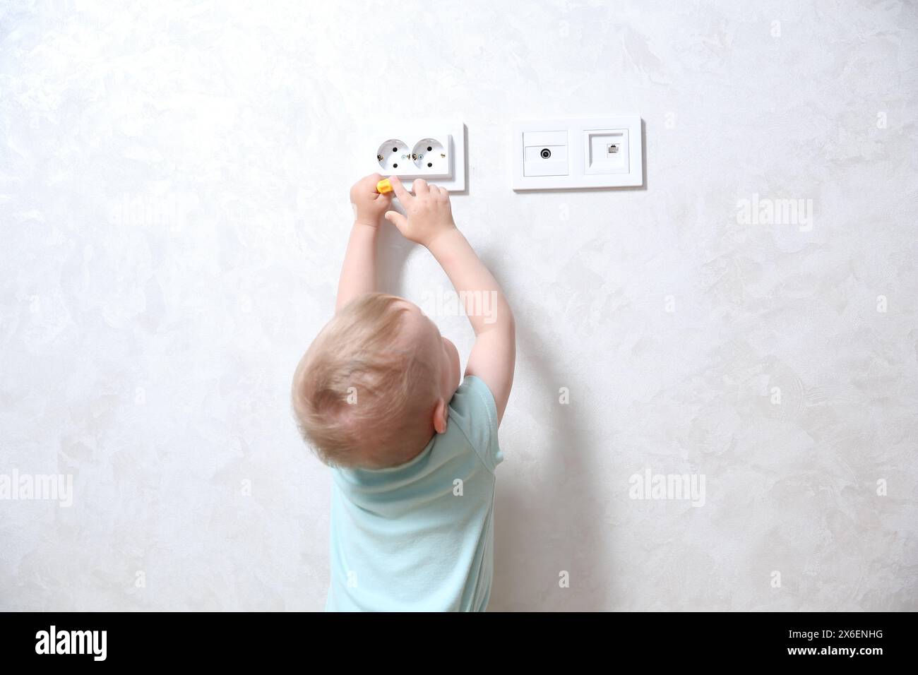 Little child playing with electrical socket indoors, back view ...