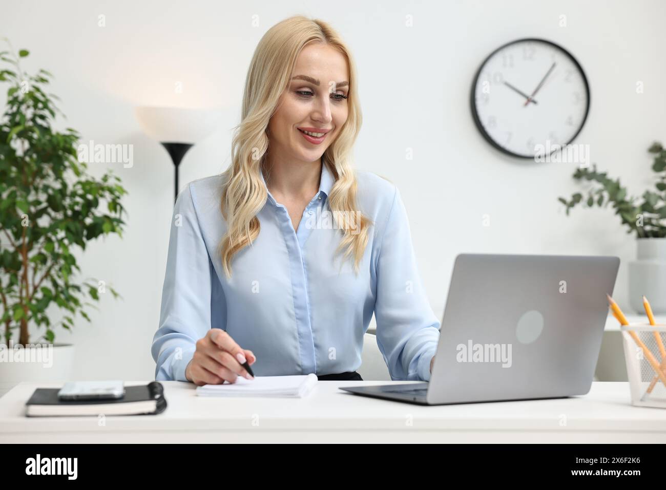 Happy secretary taking notes while working with laptop in office Stock ...