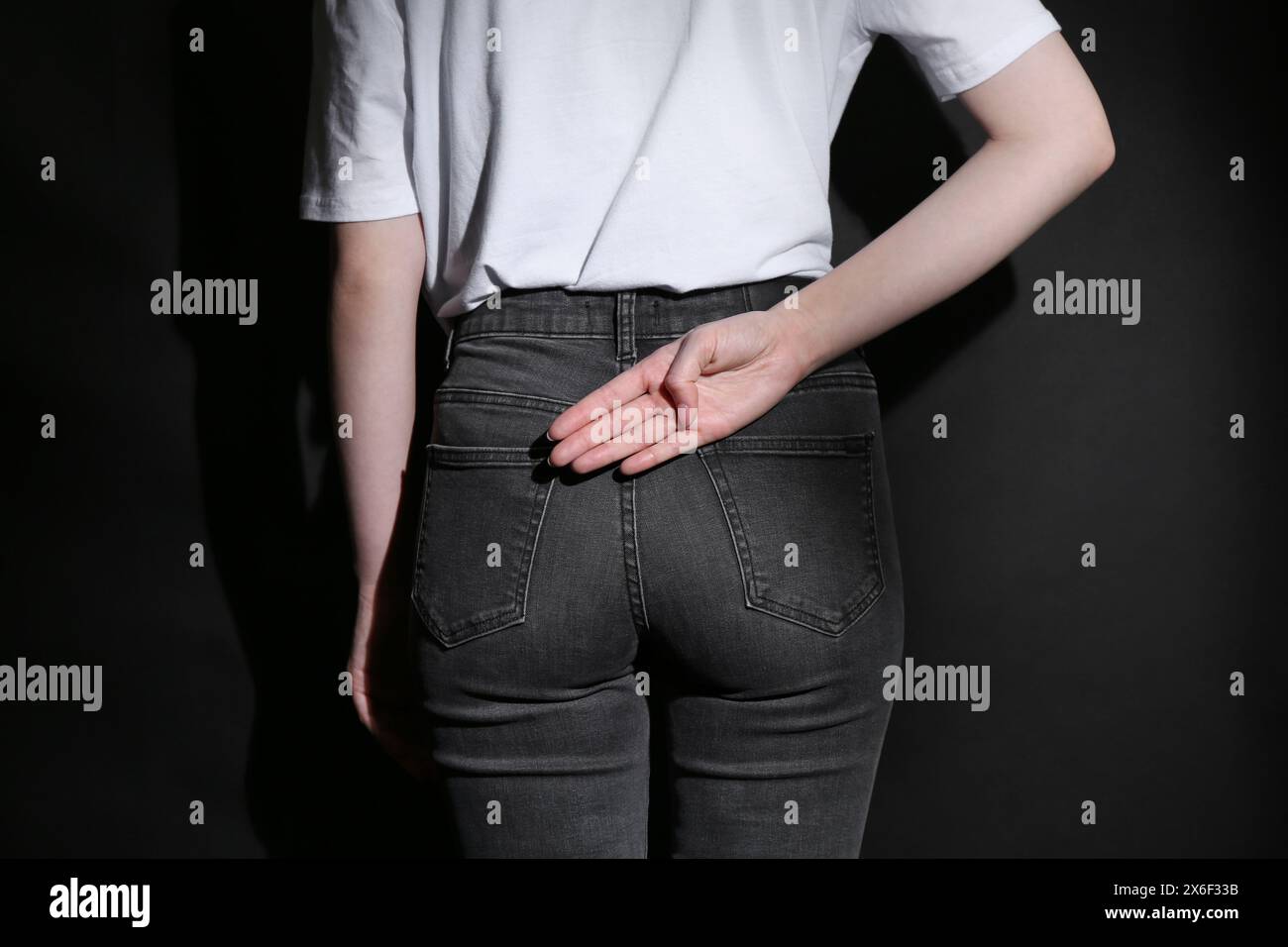 Woman showing open palm behind her back on black background, back view ...