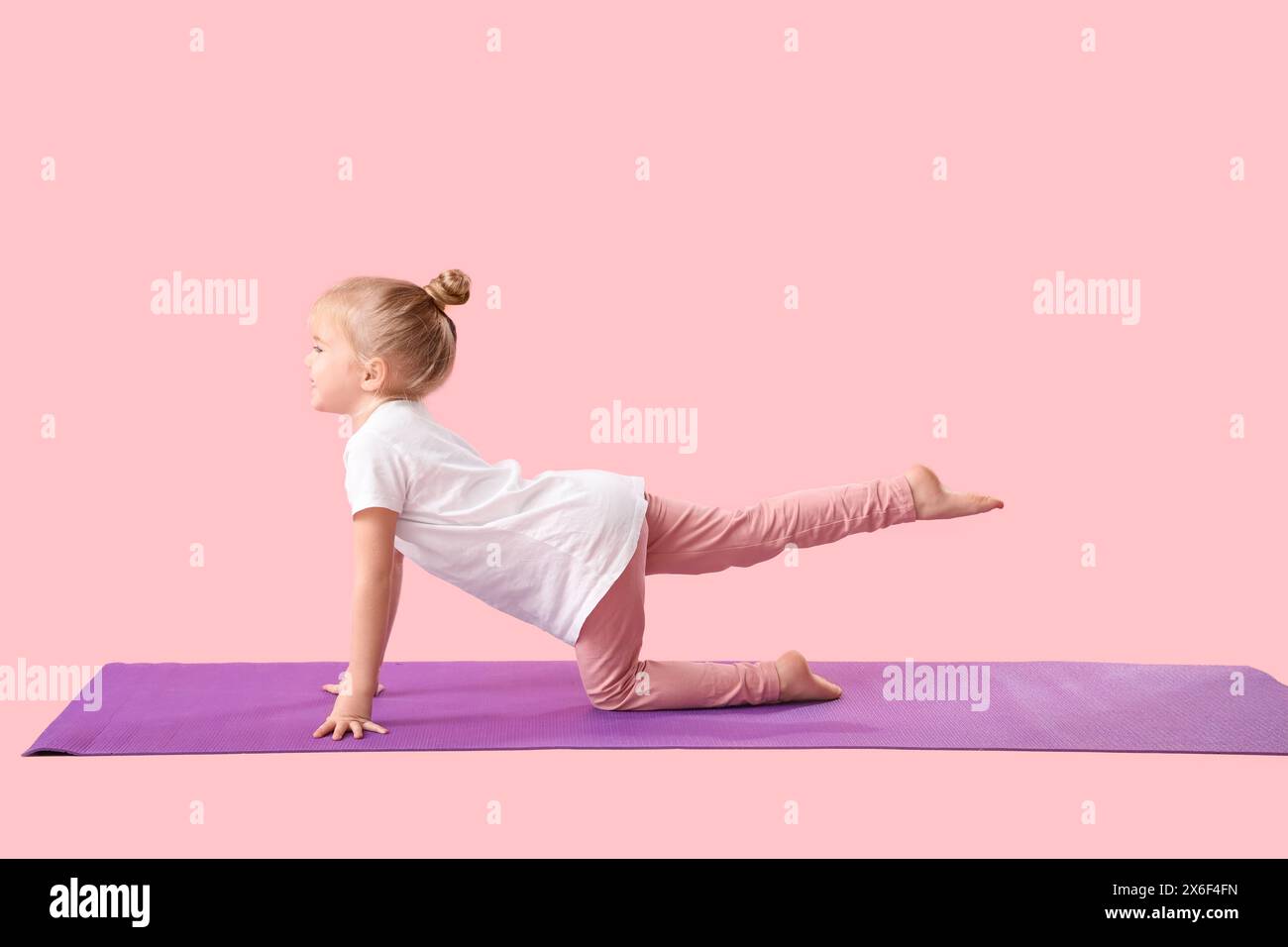 Cute little girl practicing yoga on mat against pink background Stock ...
