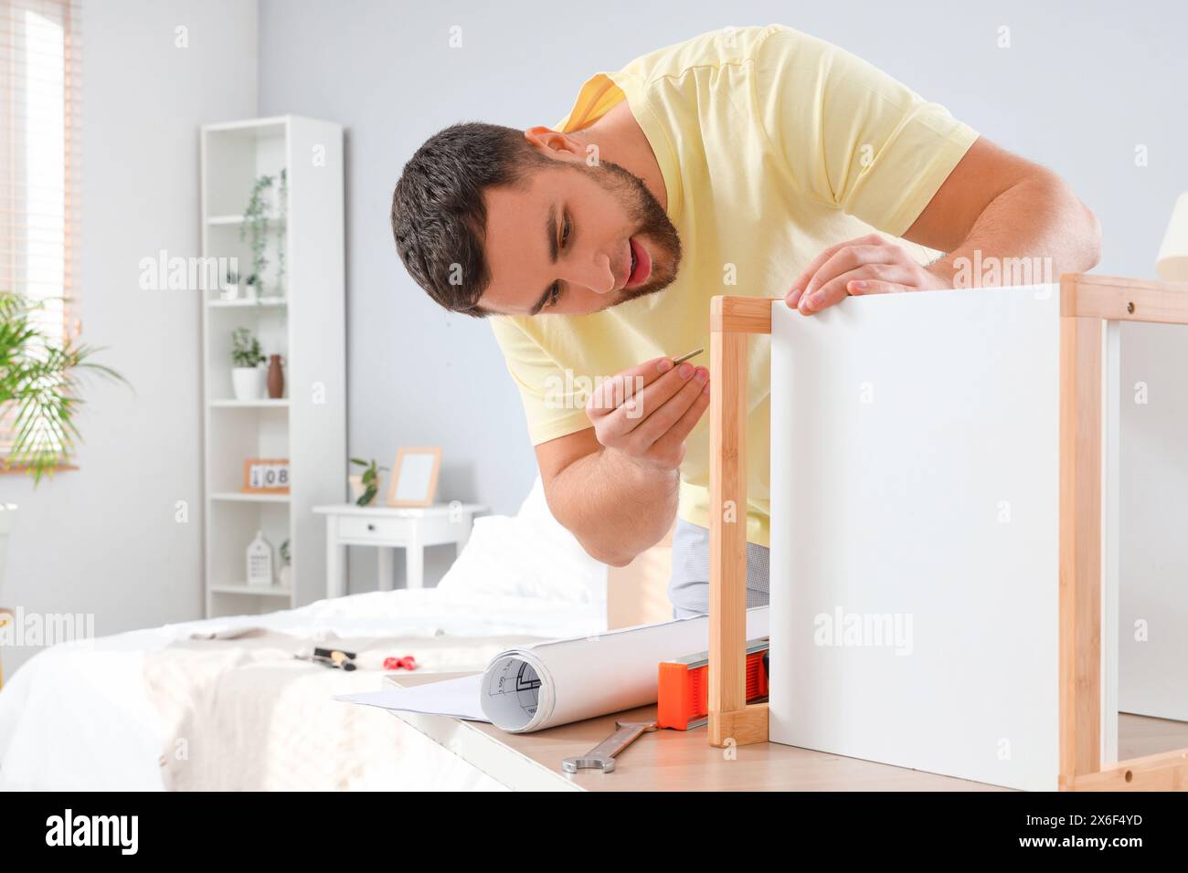 Young man assembling shelving unit in bedroom Stock Photo - Alamy