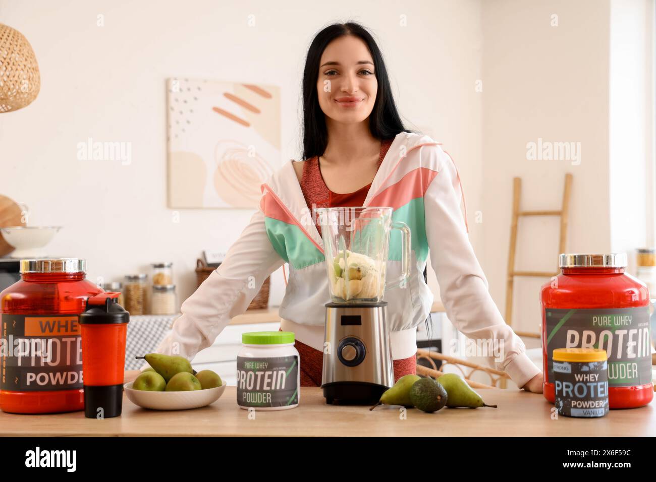 Sporty young woman preparing protein shake with blender in kitchen ...