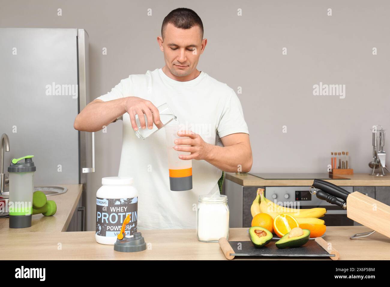 Sporty muscular man pouring water into bottle for protein shake in ...