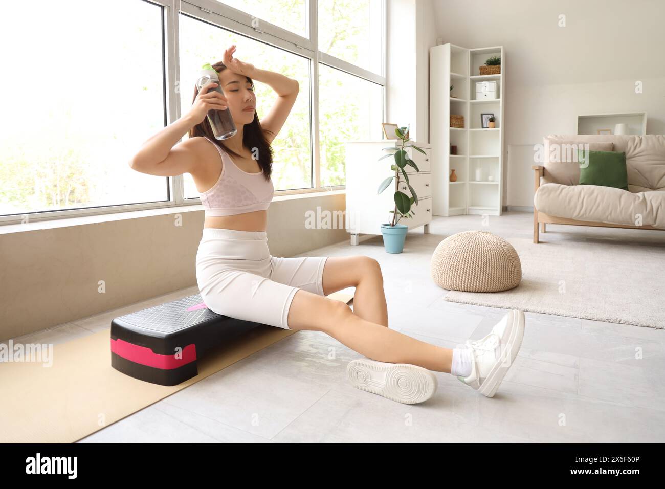 Tired sporty Asian woman putting bottle of water to her head after ...