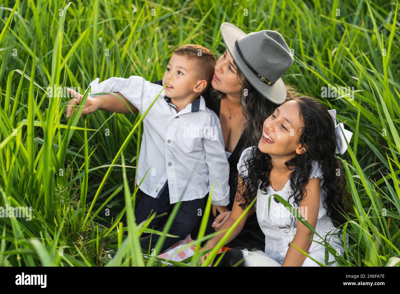Latin family, young mother with her two children sitting on the grass ...