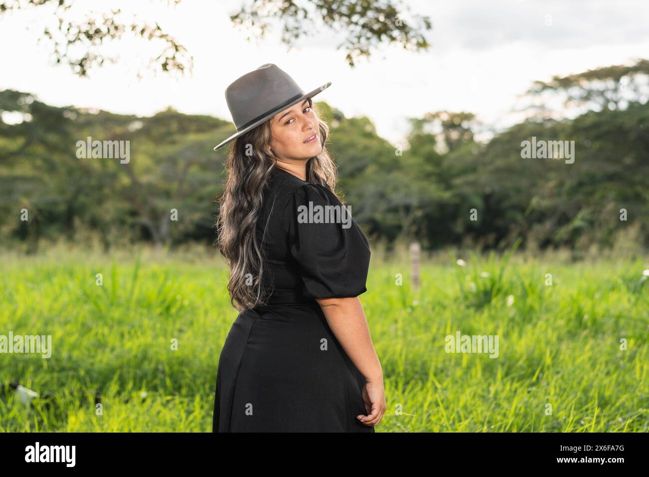 beautiful latin girl in a grass field looking back, with a sunset in ...