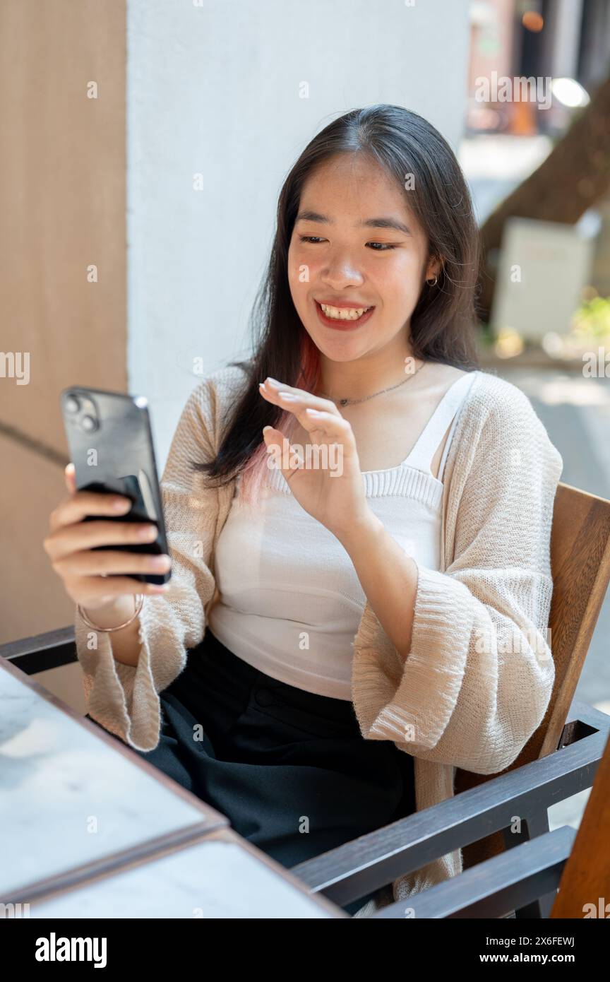 A cheerful Asian woman enjoys talking on a video call with her friend ...