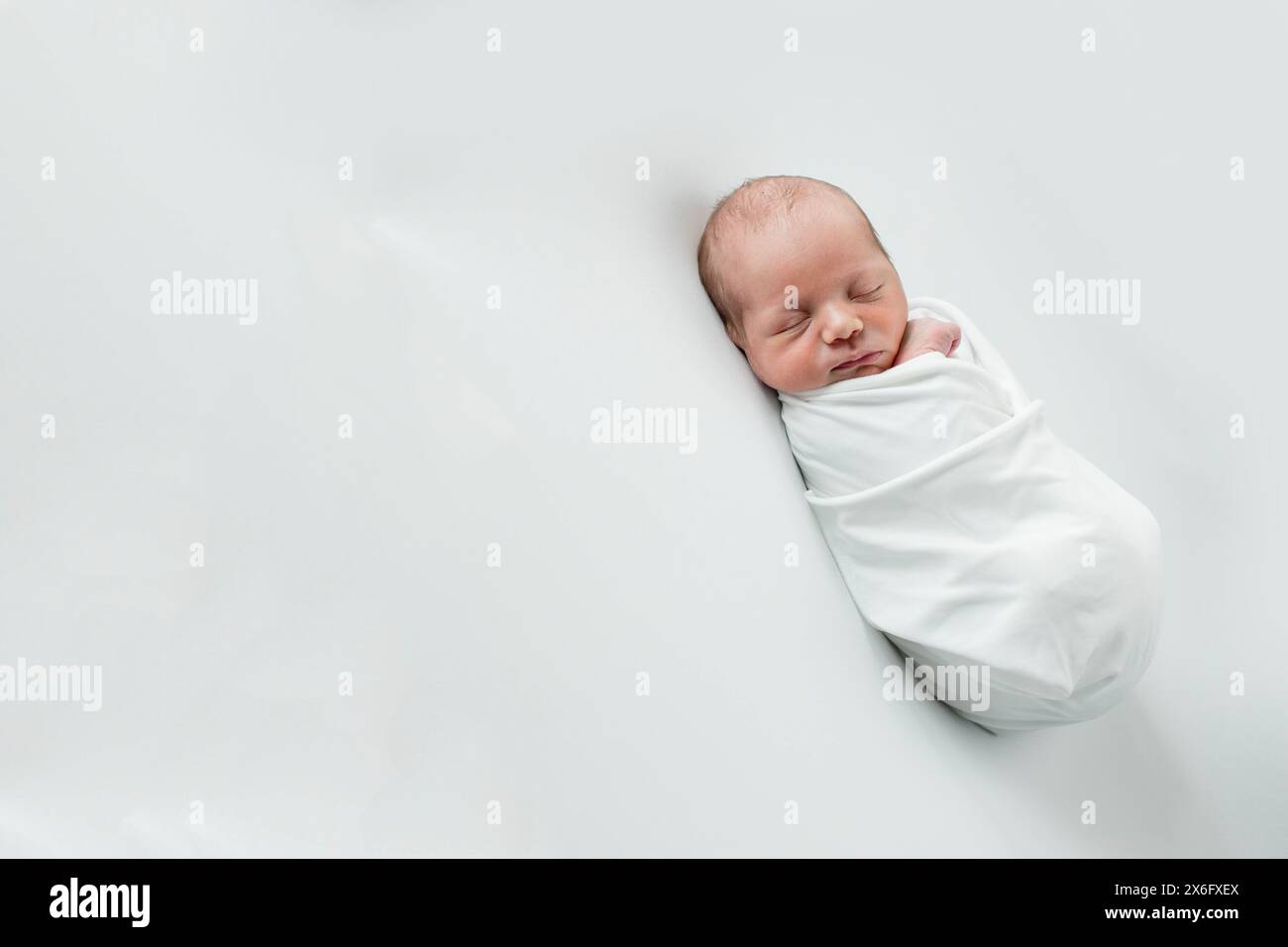 A 3-day-old baby wrapped in white cloth sleeping on a white background ...