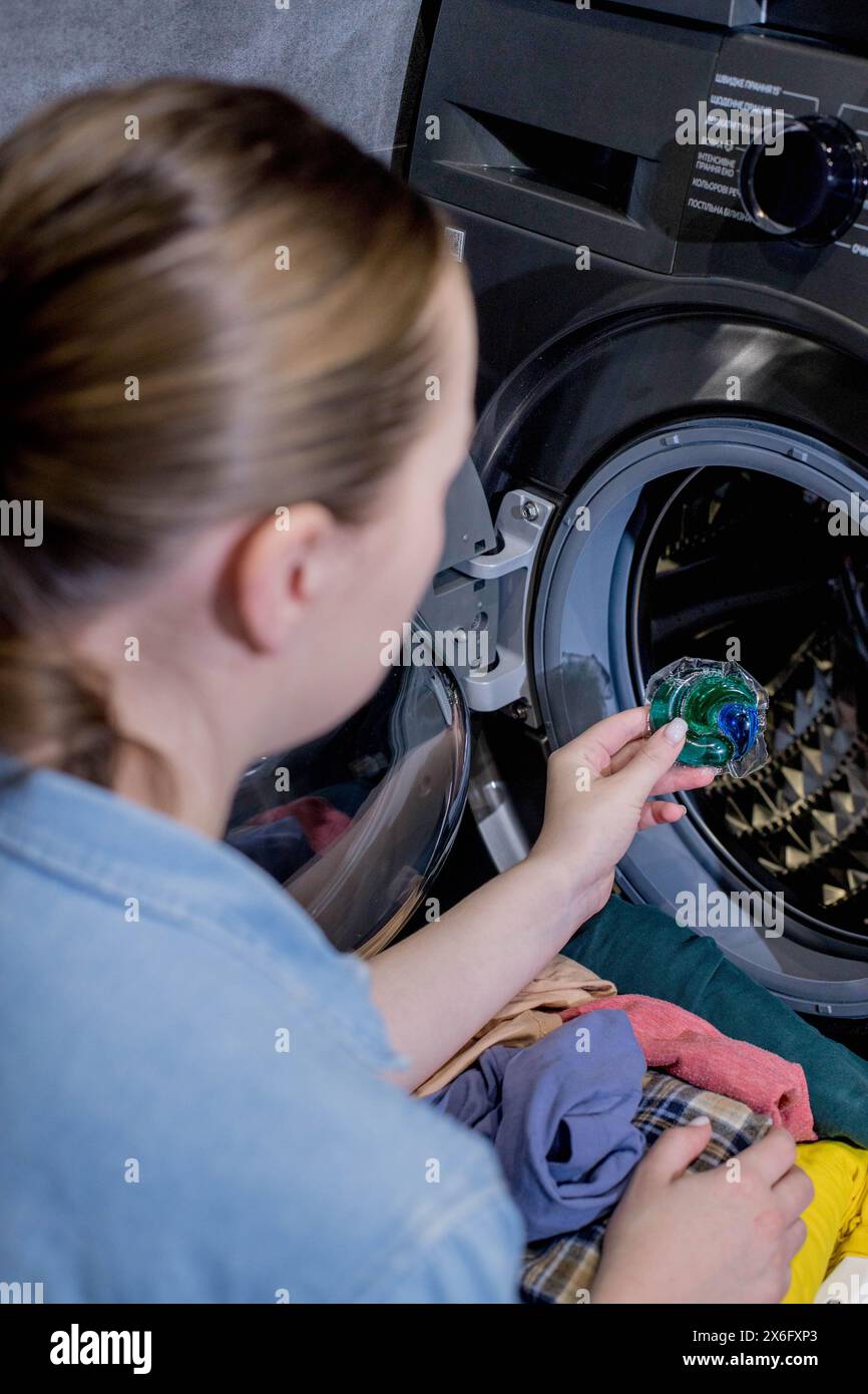 Woman putting laundry detergent capsule into washing machine indoors ...