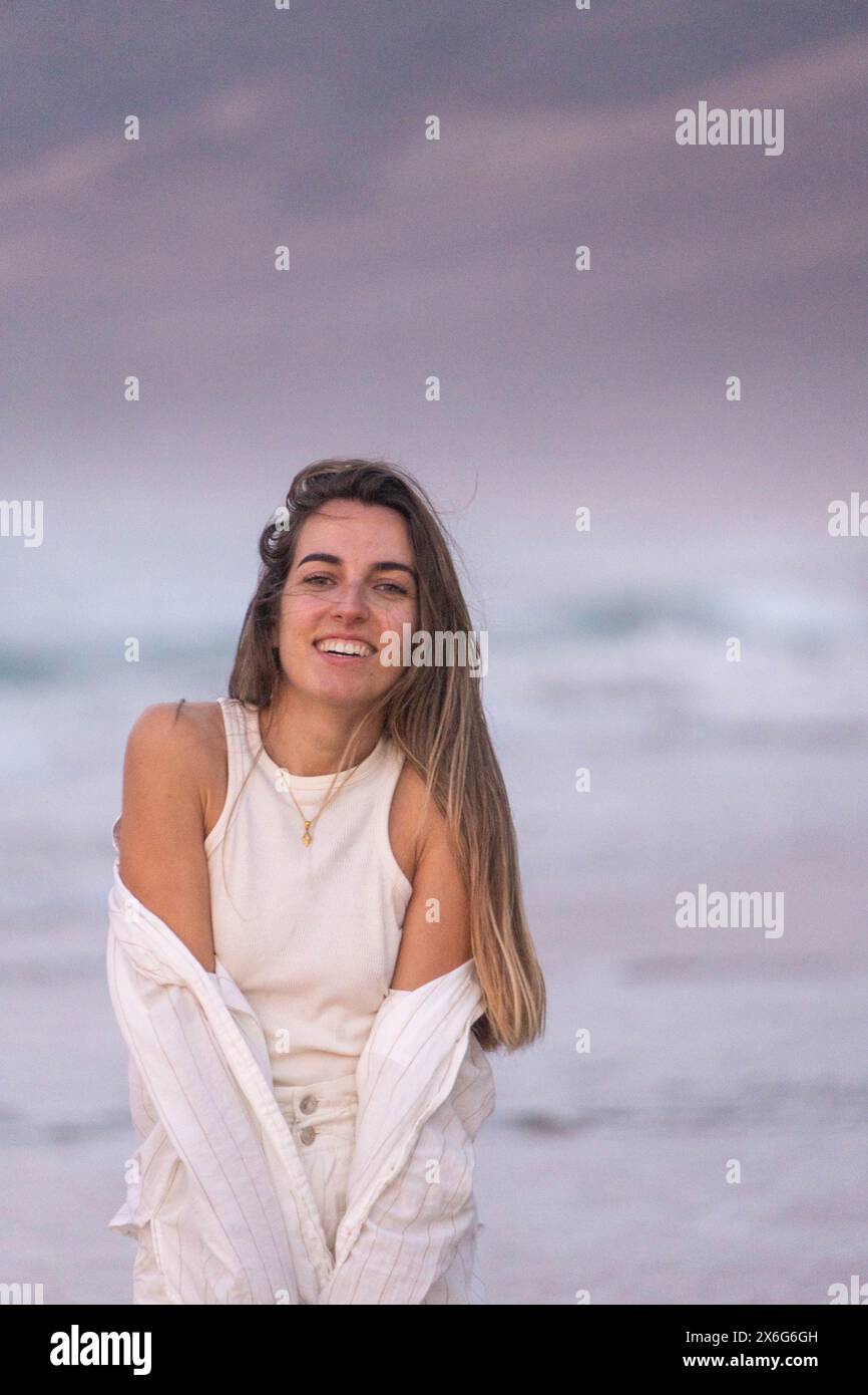 Young woman smiles gently with her arms wrapped around herself on a ...
