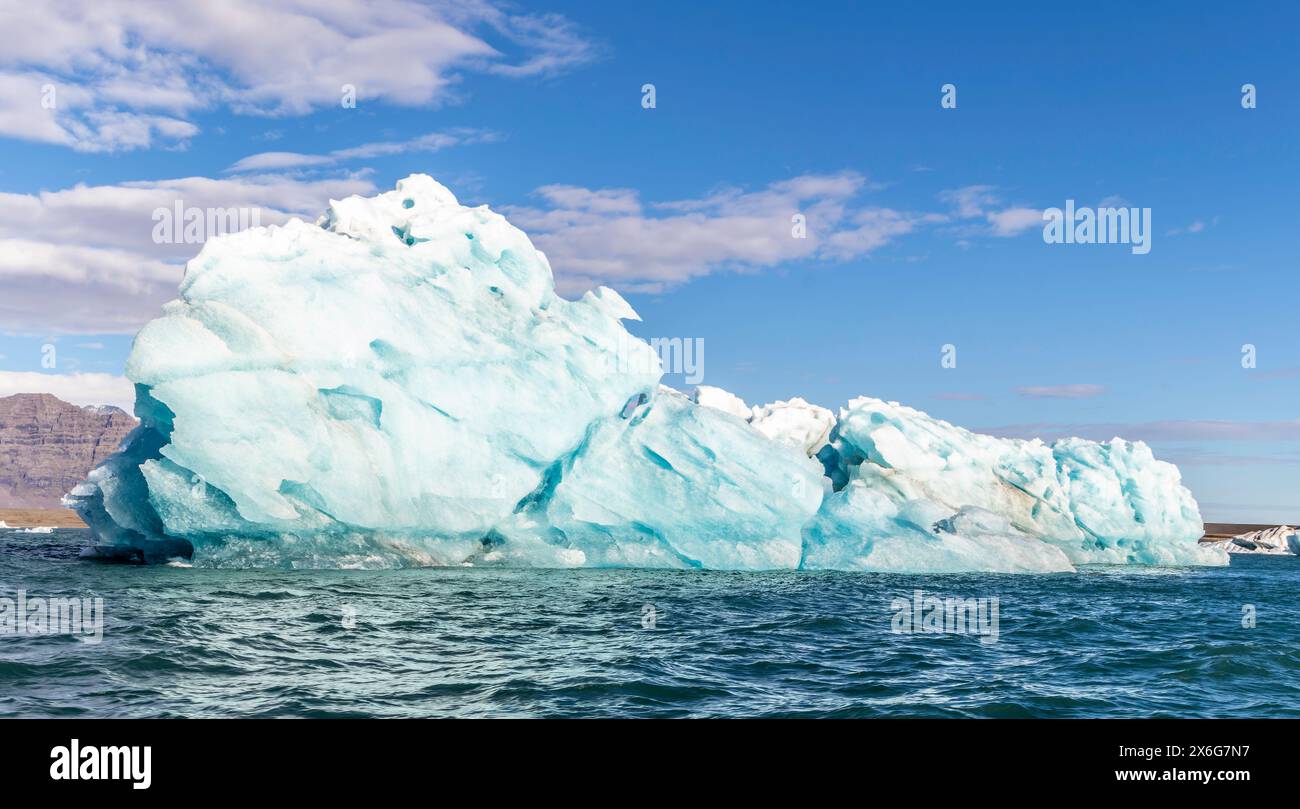 A large blue ice block floating in the ocean. The sky is clear and blue ...