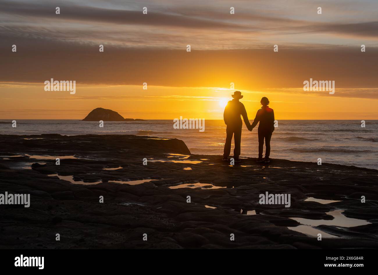 Couple holding hands and enjoying the sunset at Muriwai beach. Oaia ...