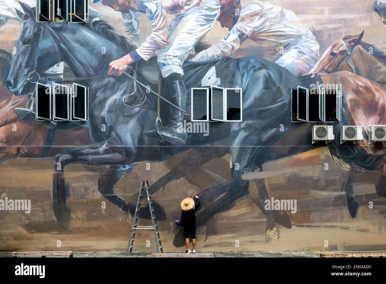 Street artist in Kuching completing a major mural of horse racing on a ...