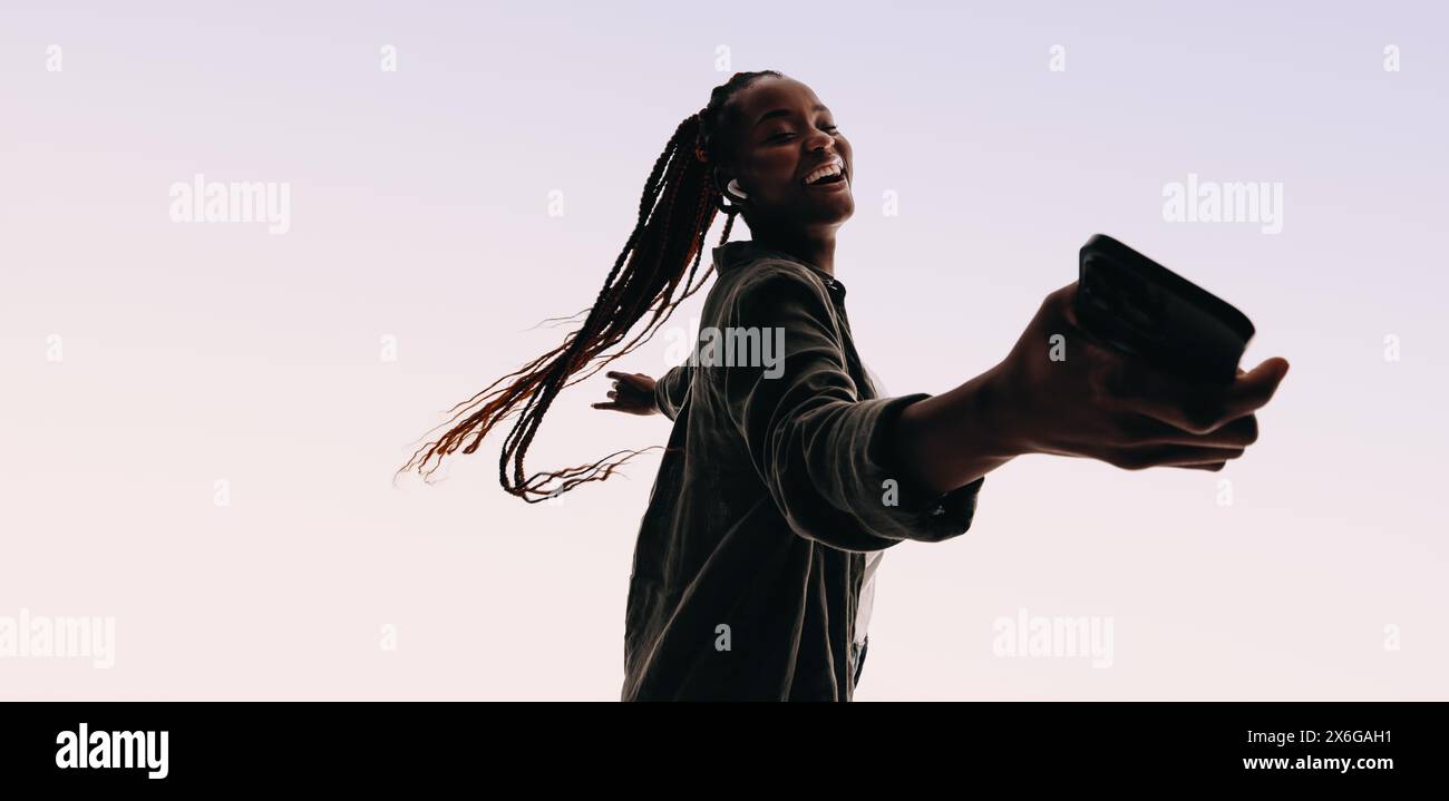 Woman dancing while holding a smartphone. She listens to music with ...