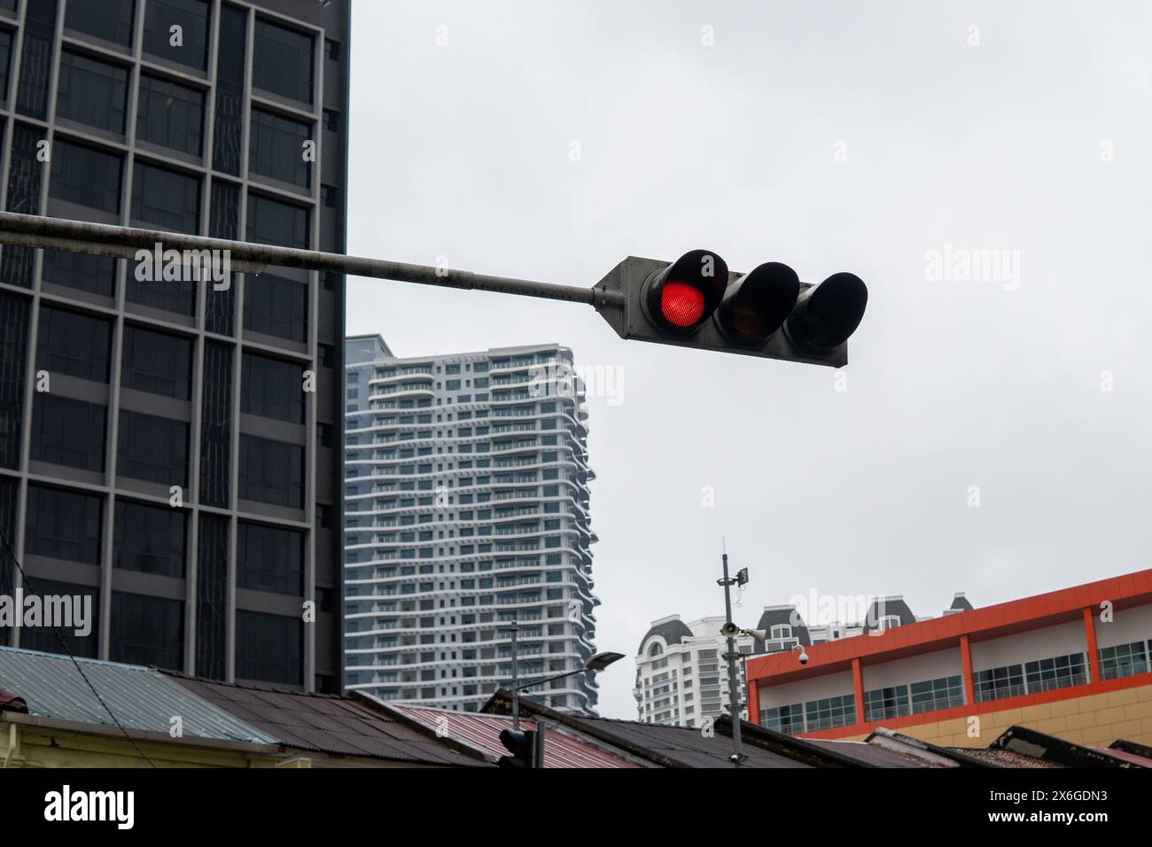 A red traffic light hangs from a pole with a background of tall, modern ...