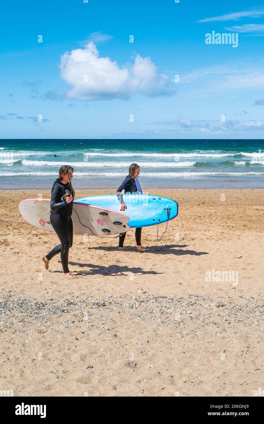 Two female surfers carrying their surfboards after surfing at Fistral ...