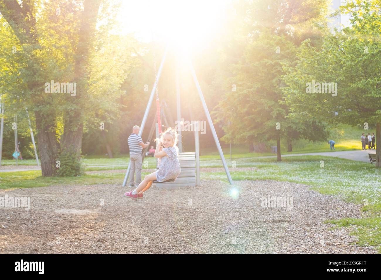 happy preschool girl swings high on summer day, blurred child figure in ...