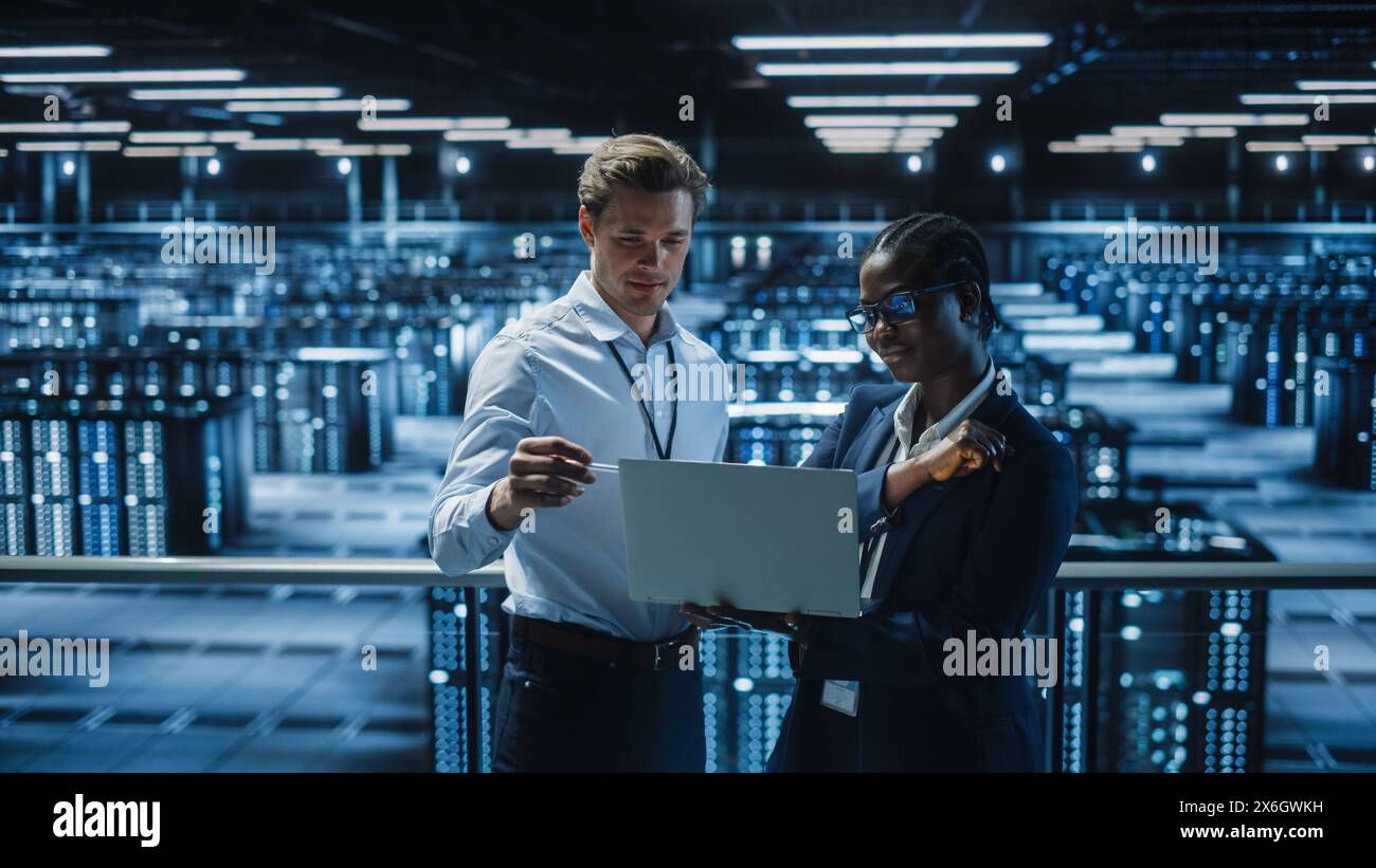 Data Center Female System Administrator and Male IT Specialist talk, Use Laptop. Information ...