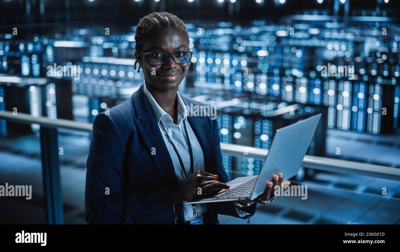 Data Center Female Programmer Using Laptop Computer Smiling And Looking At Camera In Cloud 